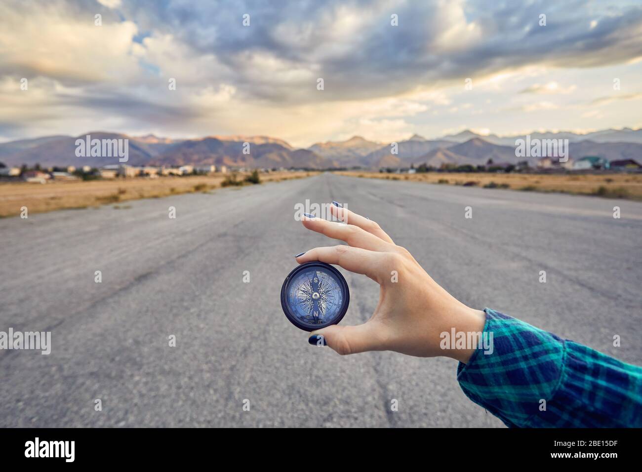 Woman hand in green shirt holding compass at sunrise sky background ...