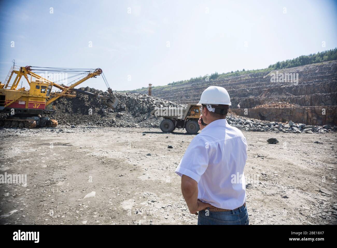 Mining engineer in white shirt and helmet supervises loading dumpers in ...