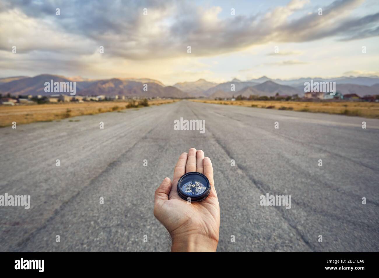 Traveler holding compass on the road with mountains at sunrise sky ...