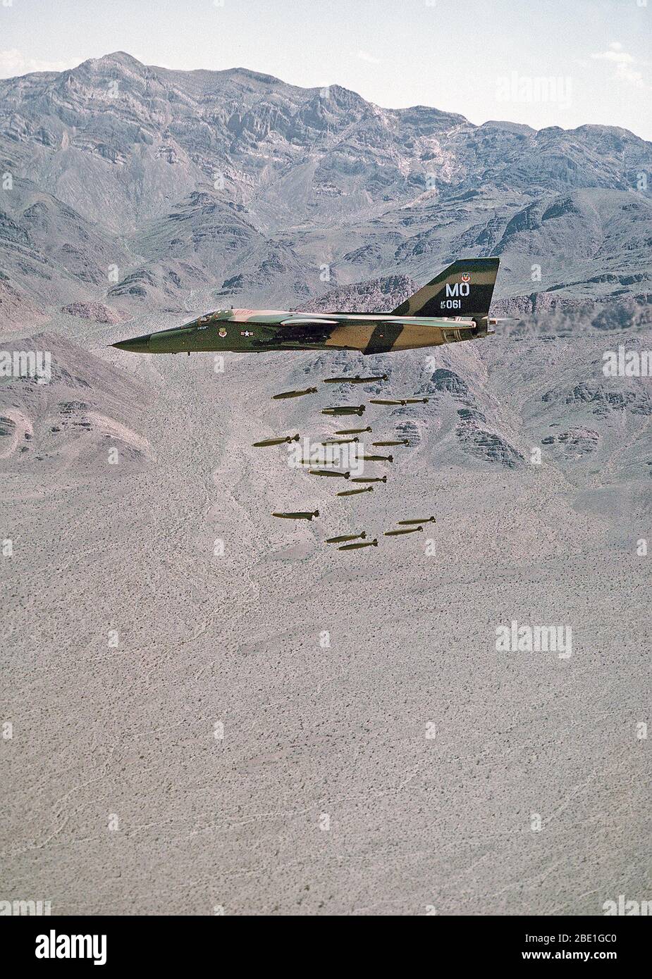 1980 - A left side view of an F-111A dropping 24 Mark 82 low-drag bombs ...