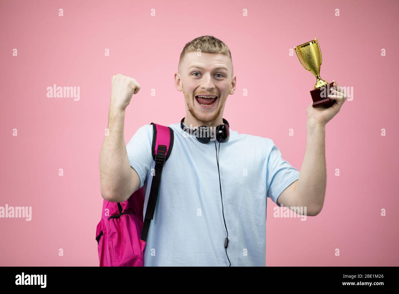 Happy student celebrates his victory with his hands up and holds cup in ...