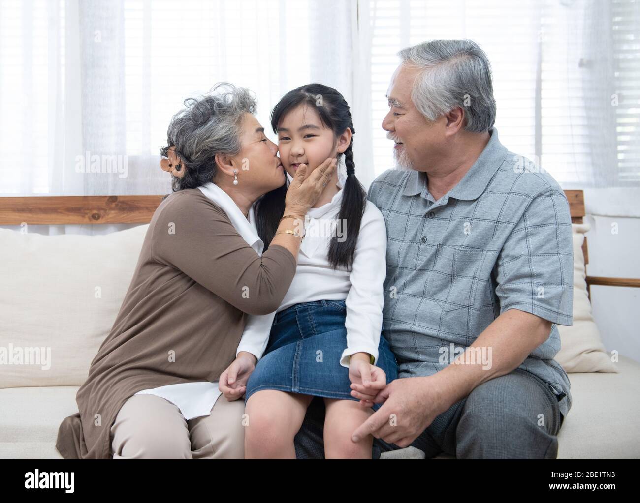 Happy asian grandparents sitting on sofa at home playing and kiss on ...