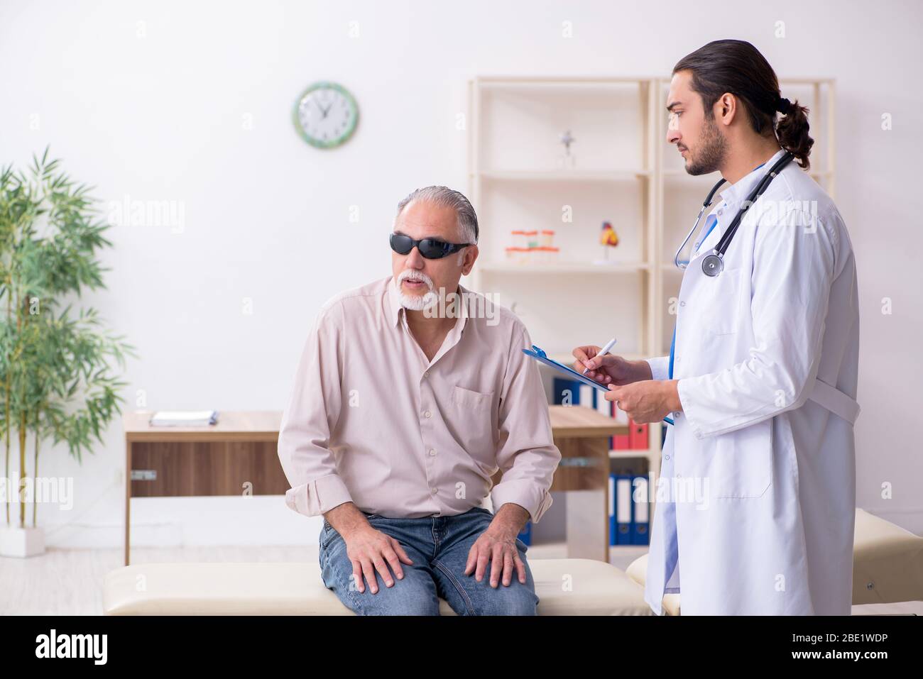 Old man visiting young male doctor Stock Photo - Alamy