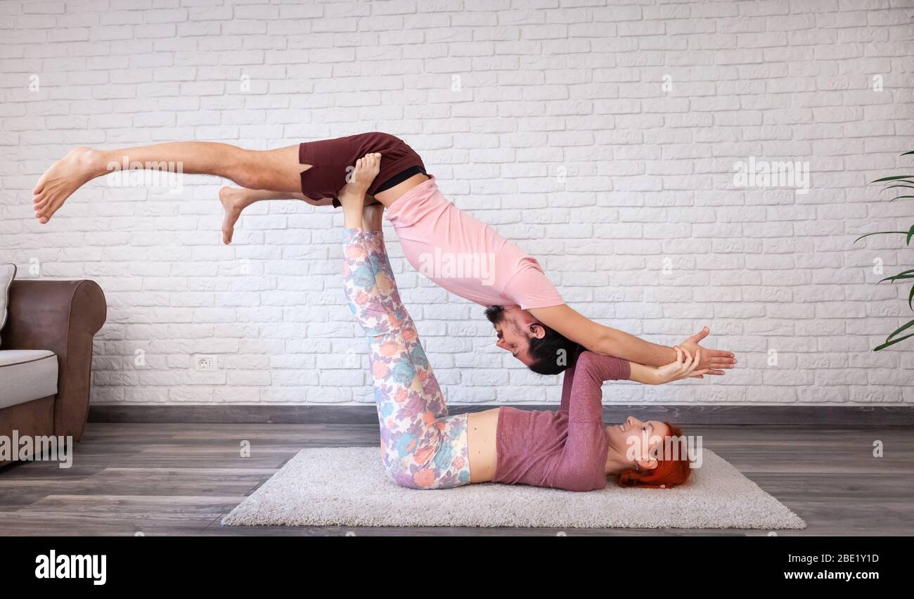 Young couple having fun at home with some acro yoga poses in different ...