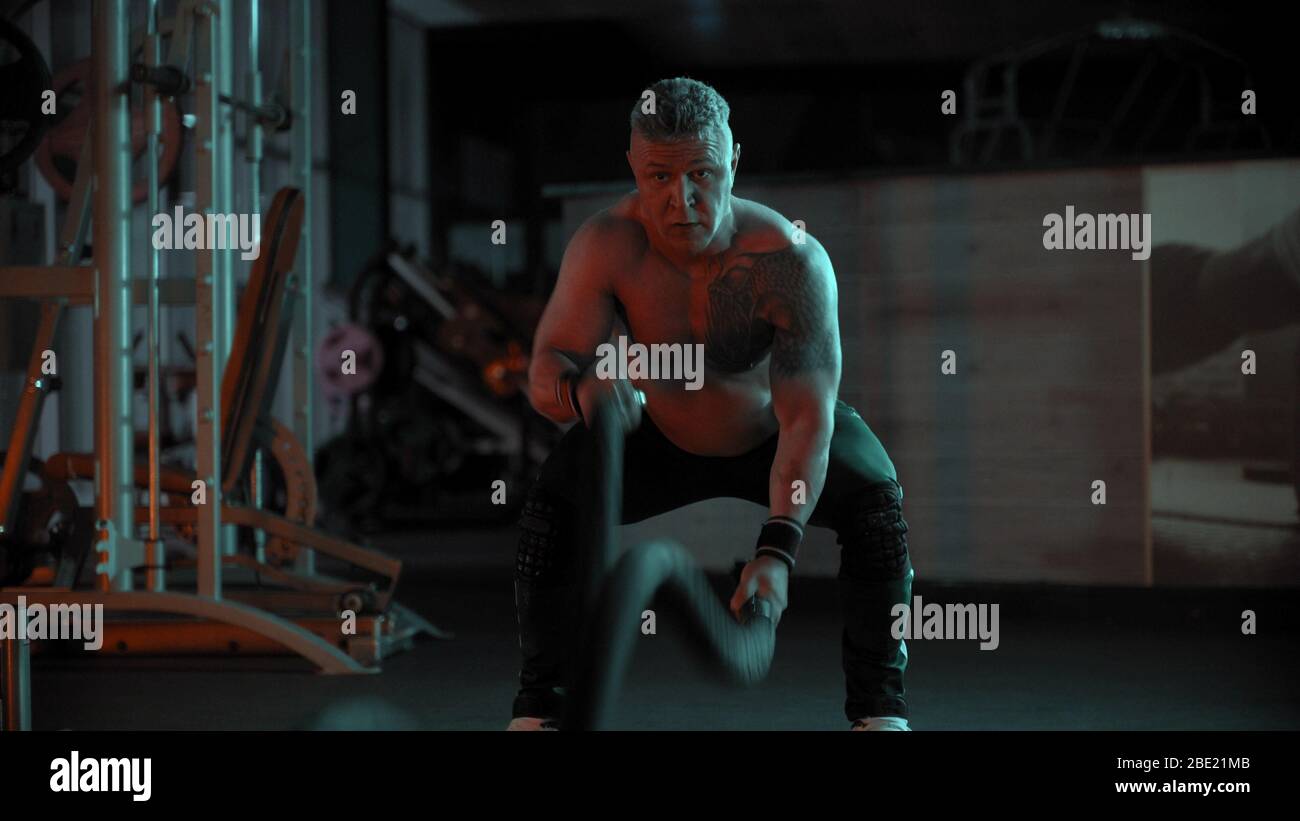 A tough man bodybuilder battling ropes in the neon lighting. Mid shot ...