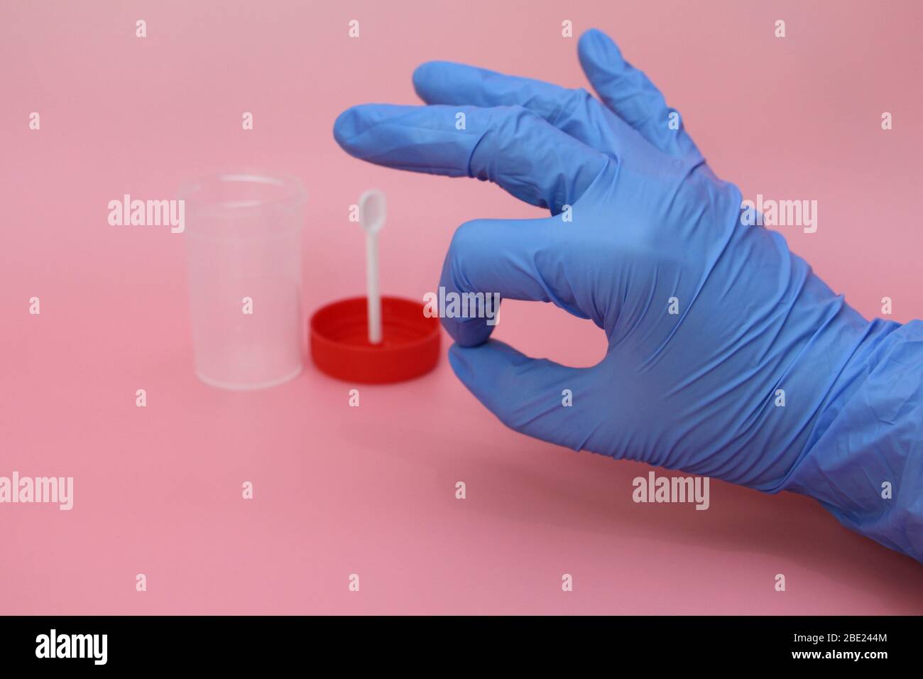 A hand in a blue latex glove holds a container for collecting feces ...