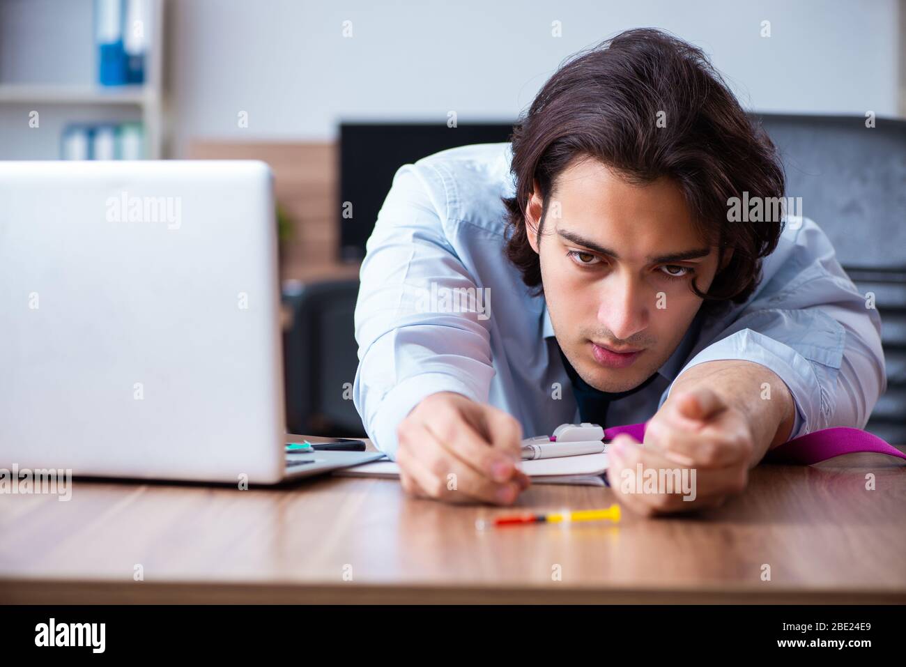The young man having problems with narcotics at workplace Stock Photo ...