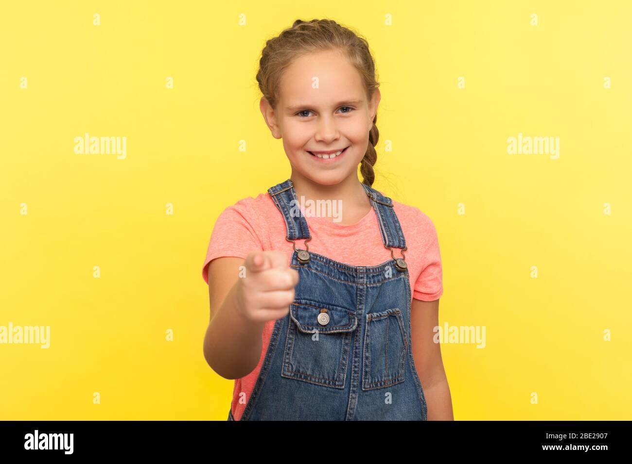 Hey you! Portrait of happy little girl with braid in denim overalls ...