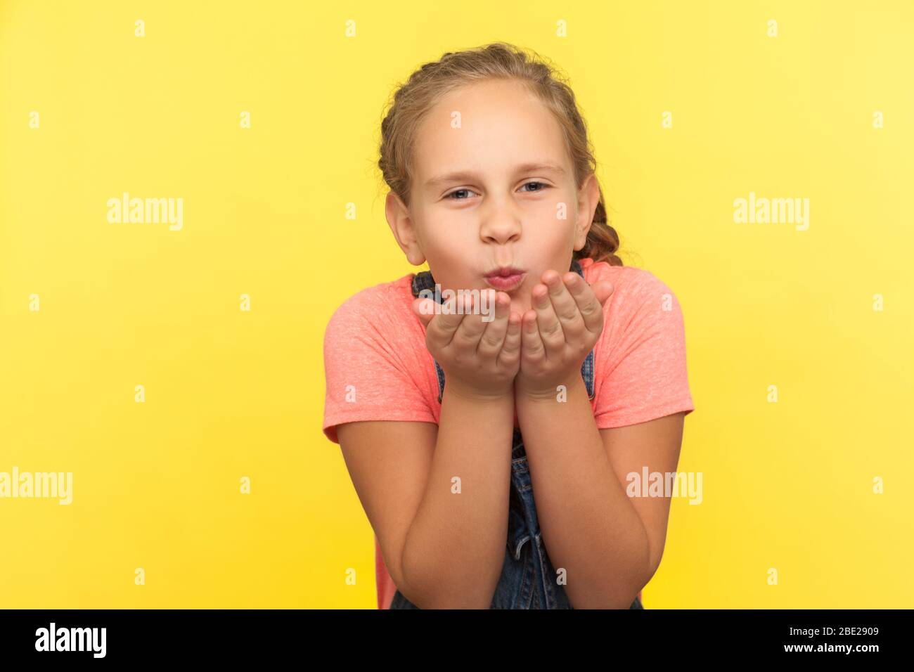 Portrait of charming sweet little girl with braid in denim overalls ...