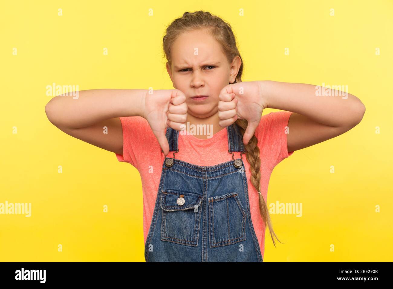 Dislike. Portrait of displeased upset little girl with braid in denim ...