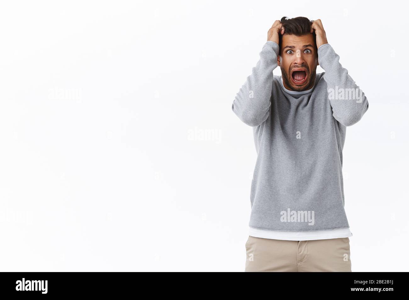 Scared guy in panic grab head and screaming, stare camera popped eyes from fright, afraid ...