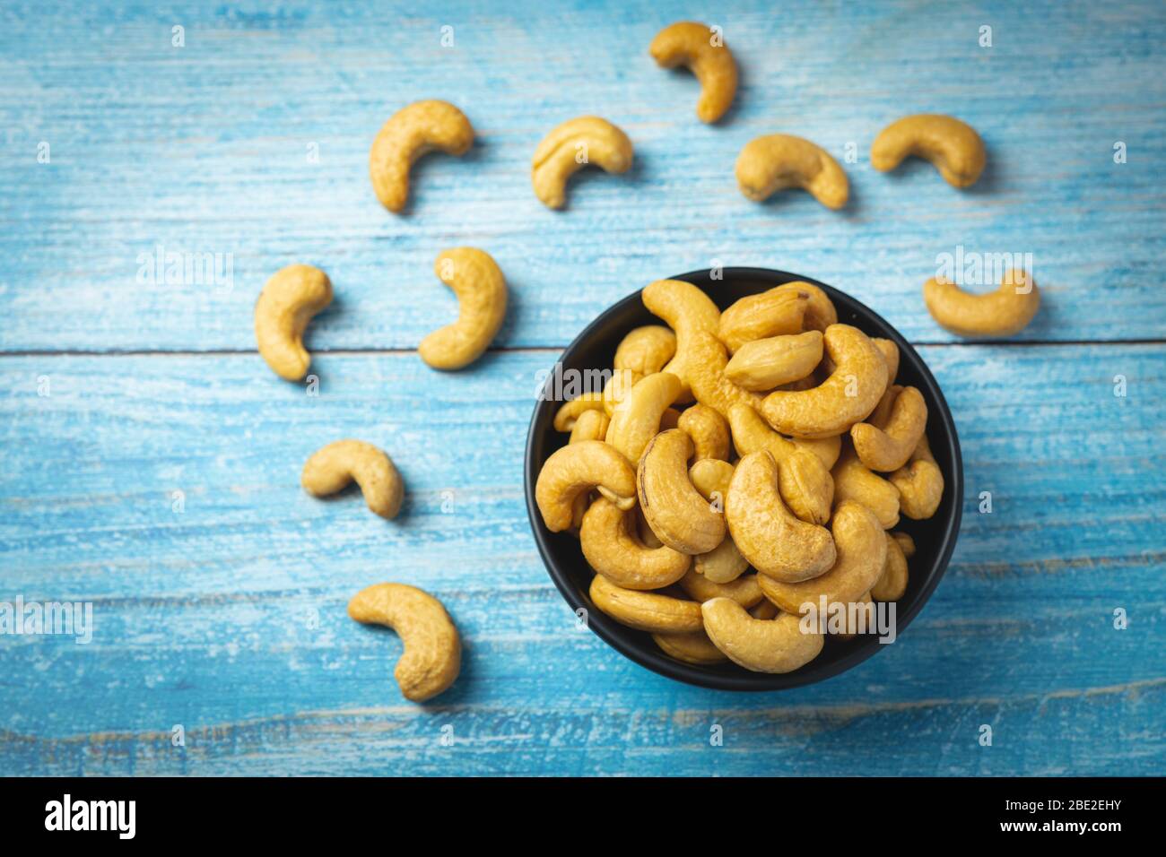 Top view of roasted cashew nut in salt in black bowl on soft blue ...