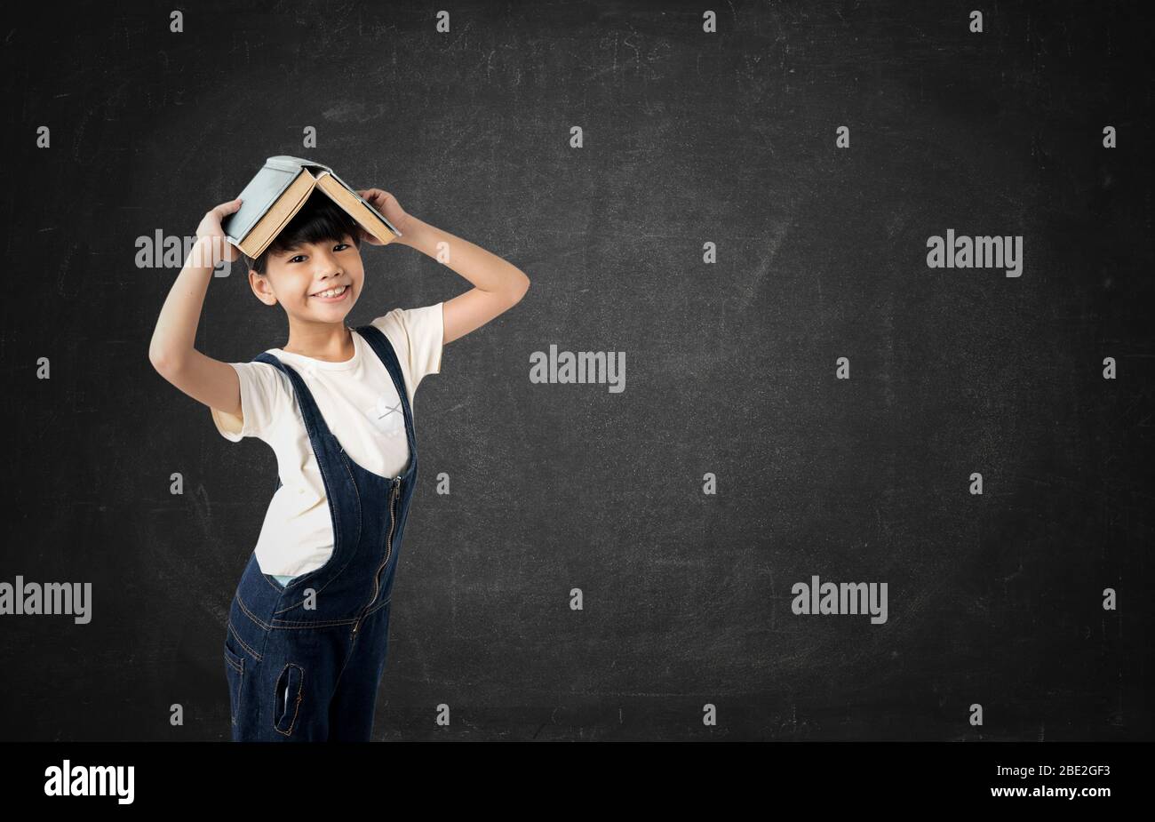 Young Asian girl student holding book over head on chalkboard ...