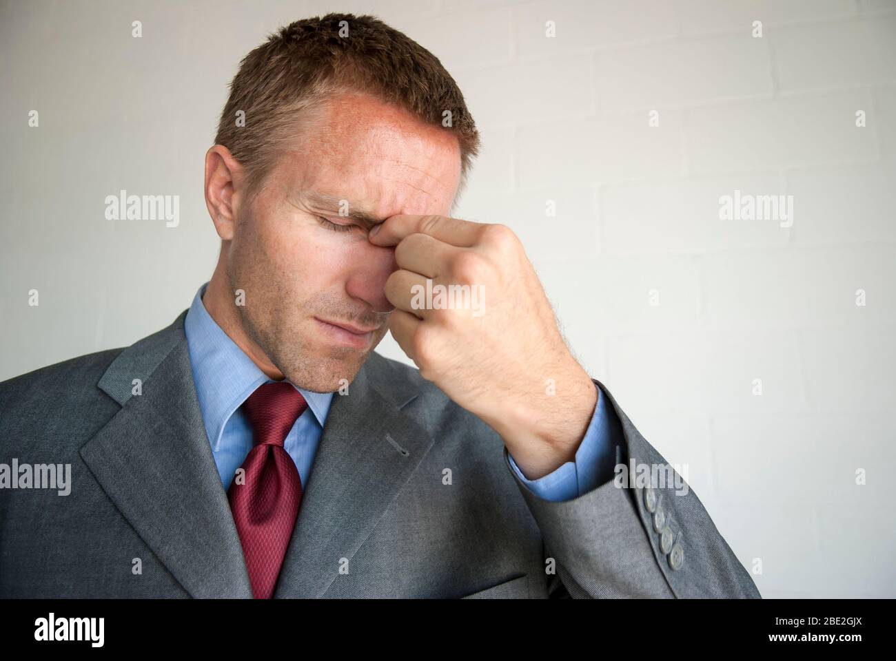 Stressed businessman pinching the bridge of his nose to alleviate his ...