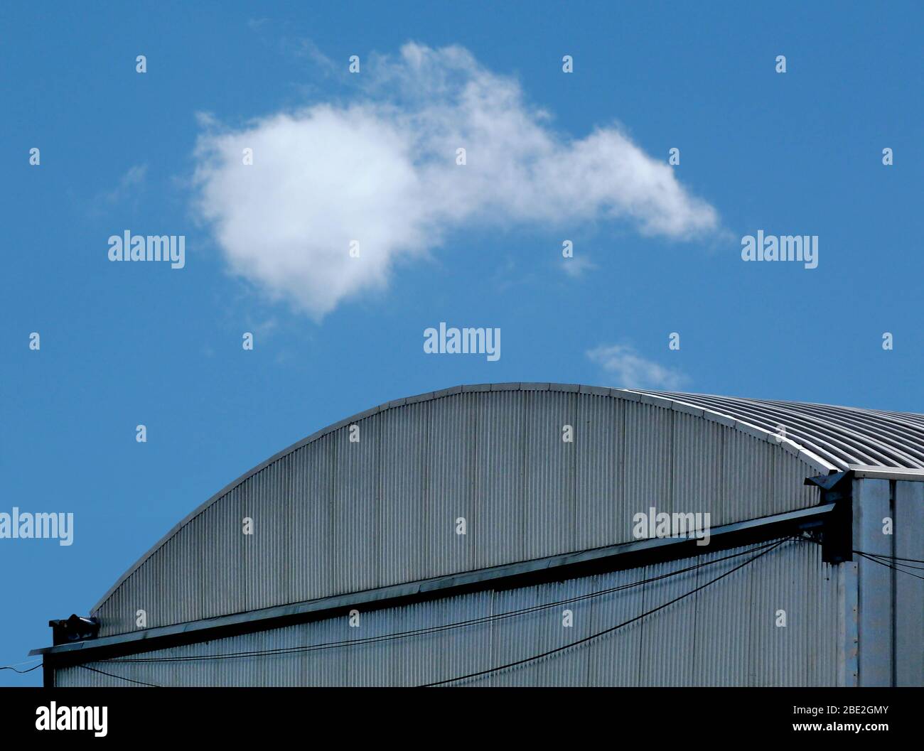 arched corrugated aluminum clad hangar building roof detail. blue sky ...