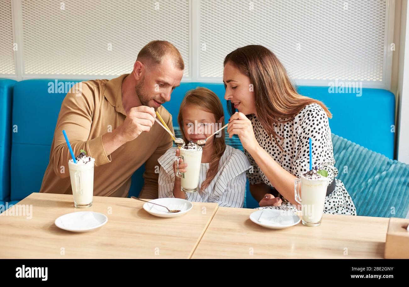 Happy family is having a milkshake break in the city cafe, mom and dad ...