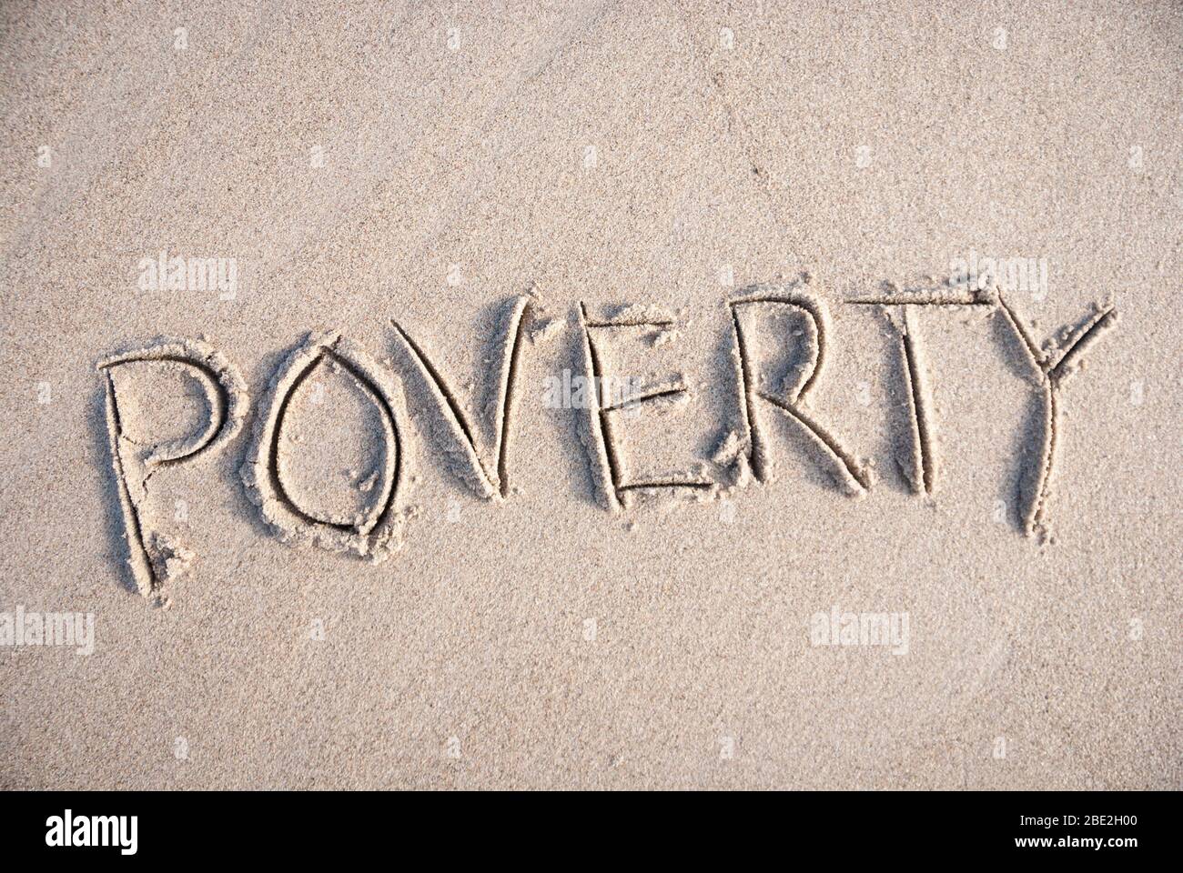 Simple message of Poverty handwritten outdoors on smooth sand beach ...