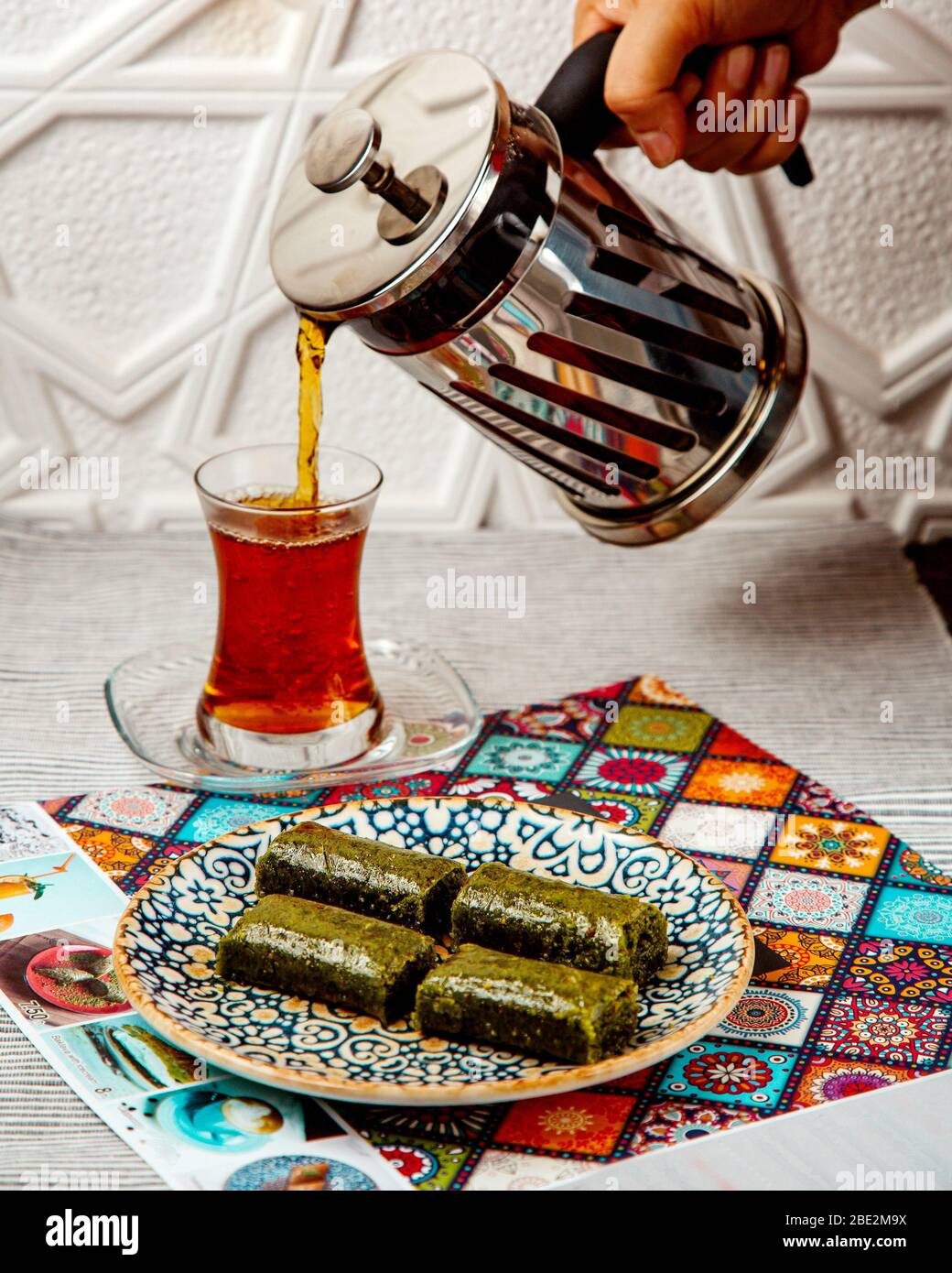 woman pouring black tea from french press served with turkish dessert ...