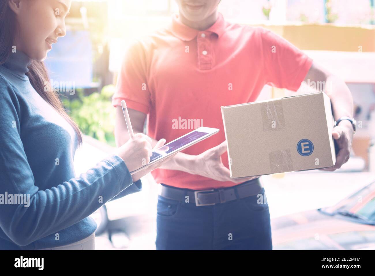 Beautiful girl receiving parcel from postman and signing on tablet that ...