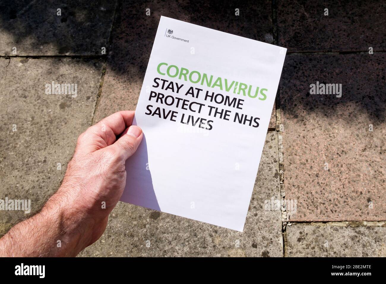 A man holds a copy of UK Government stay home protect NHS save lives ...