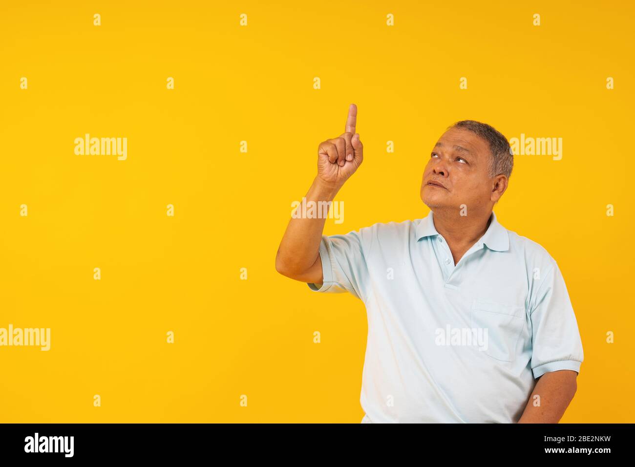 Portrait of old man pointing up on yellow background, introduce produce ...