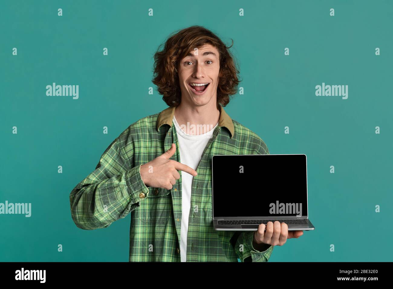 Happy millennial guy pointing at laptop computer with empty screen on ...