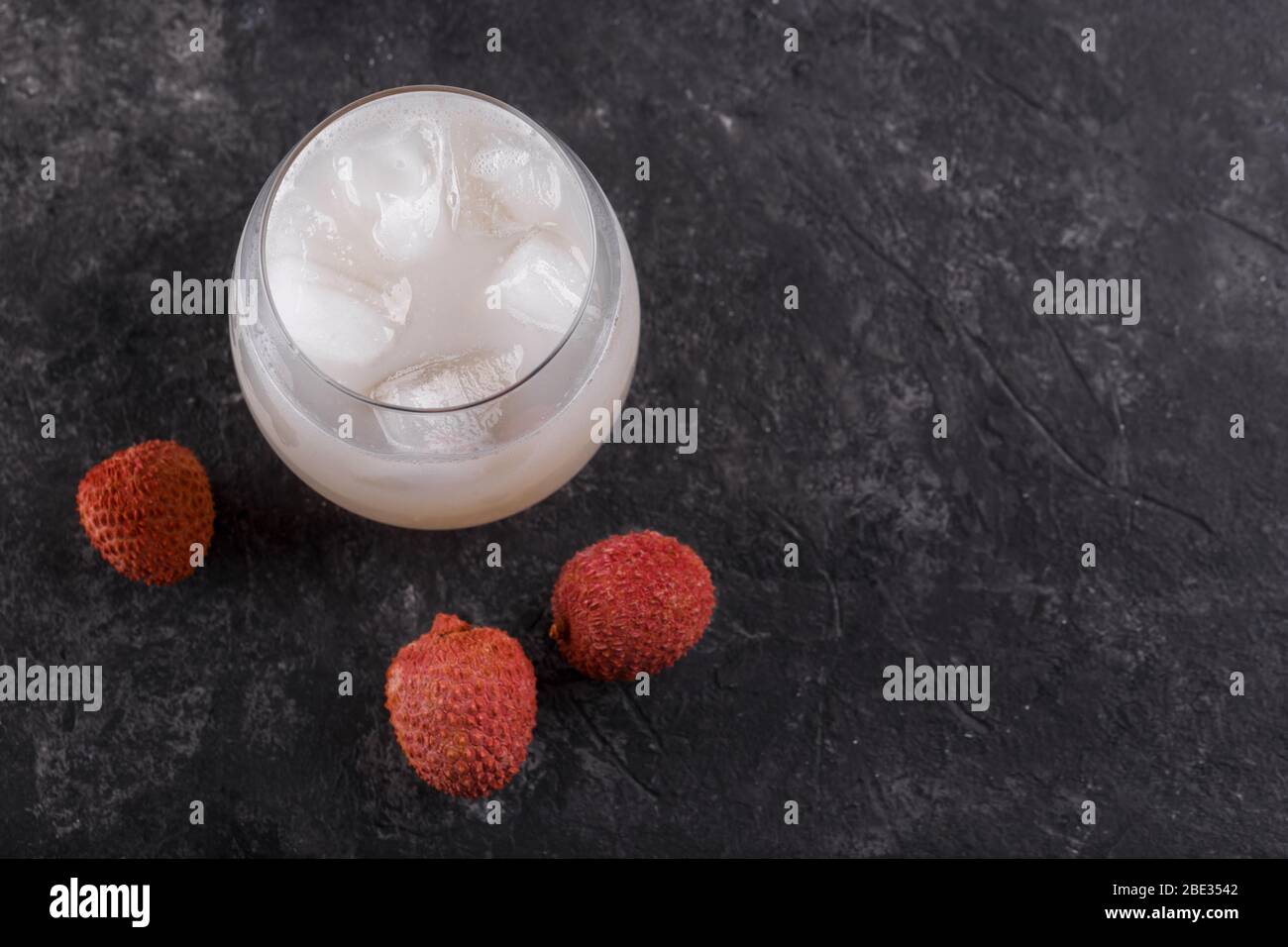 Glass of fresh cold lychee juice with ice and lemon on black stone ...