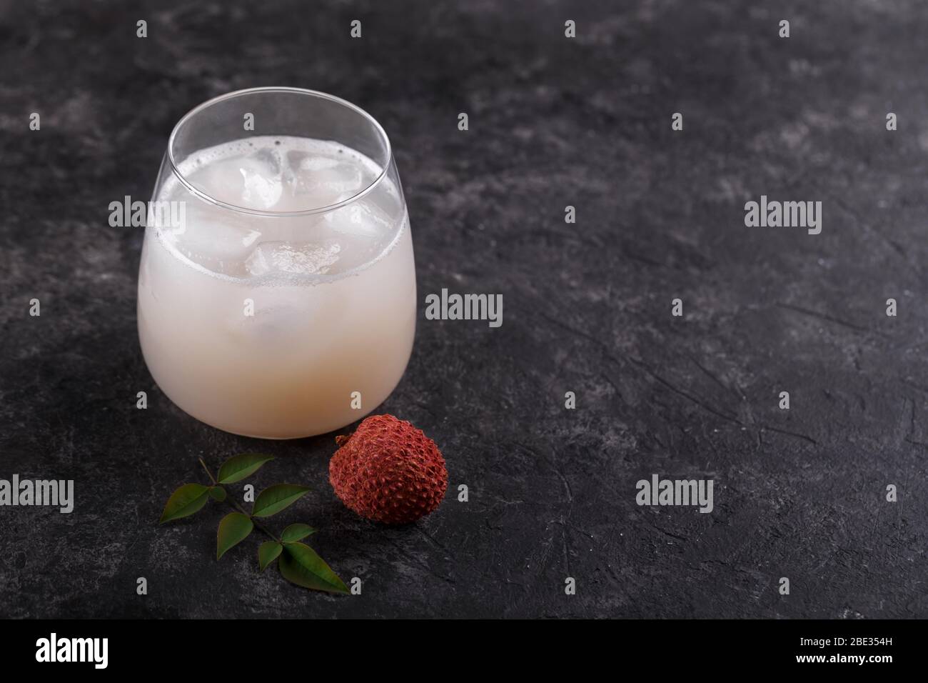Glass of fresh cold lychee juice with ice and lemon on black stone ...