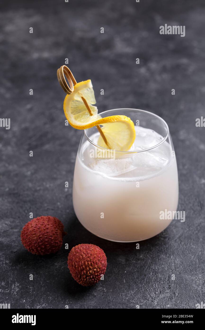 Glass of fresh cold lychee juice with ice and lemon on black stone ...