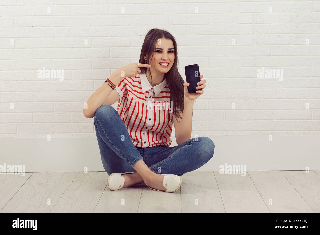 Young woman pointing finger at black blank screen smartphone, sitting ...