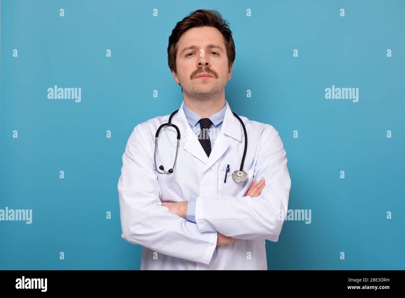 Young serious medical doctor with stethoscope posing against blue ...