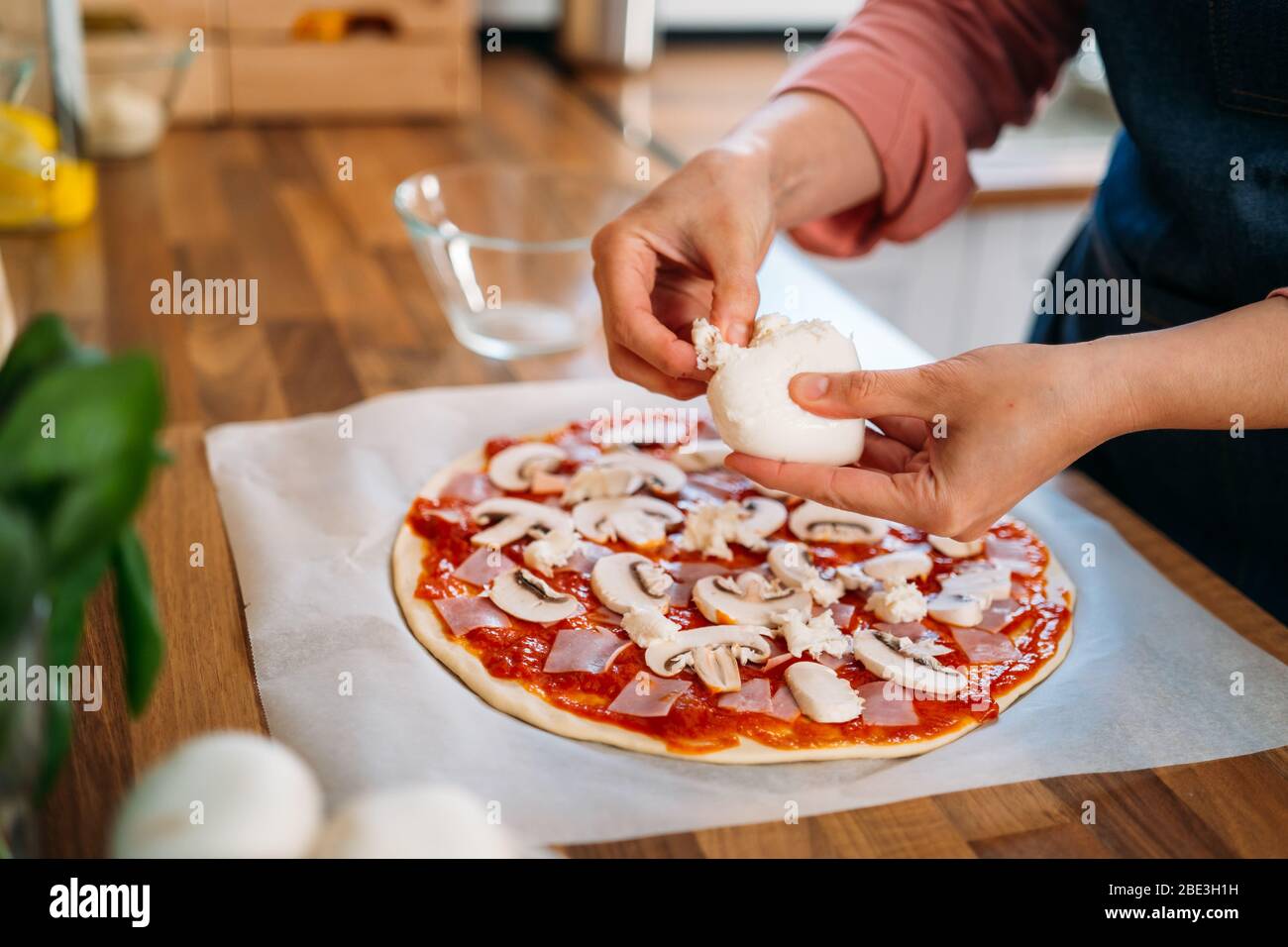 Woman's hands adding mozzarella cheese to a traditional margarita pizza ...