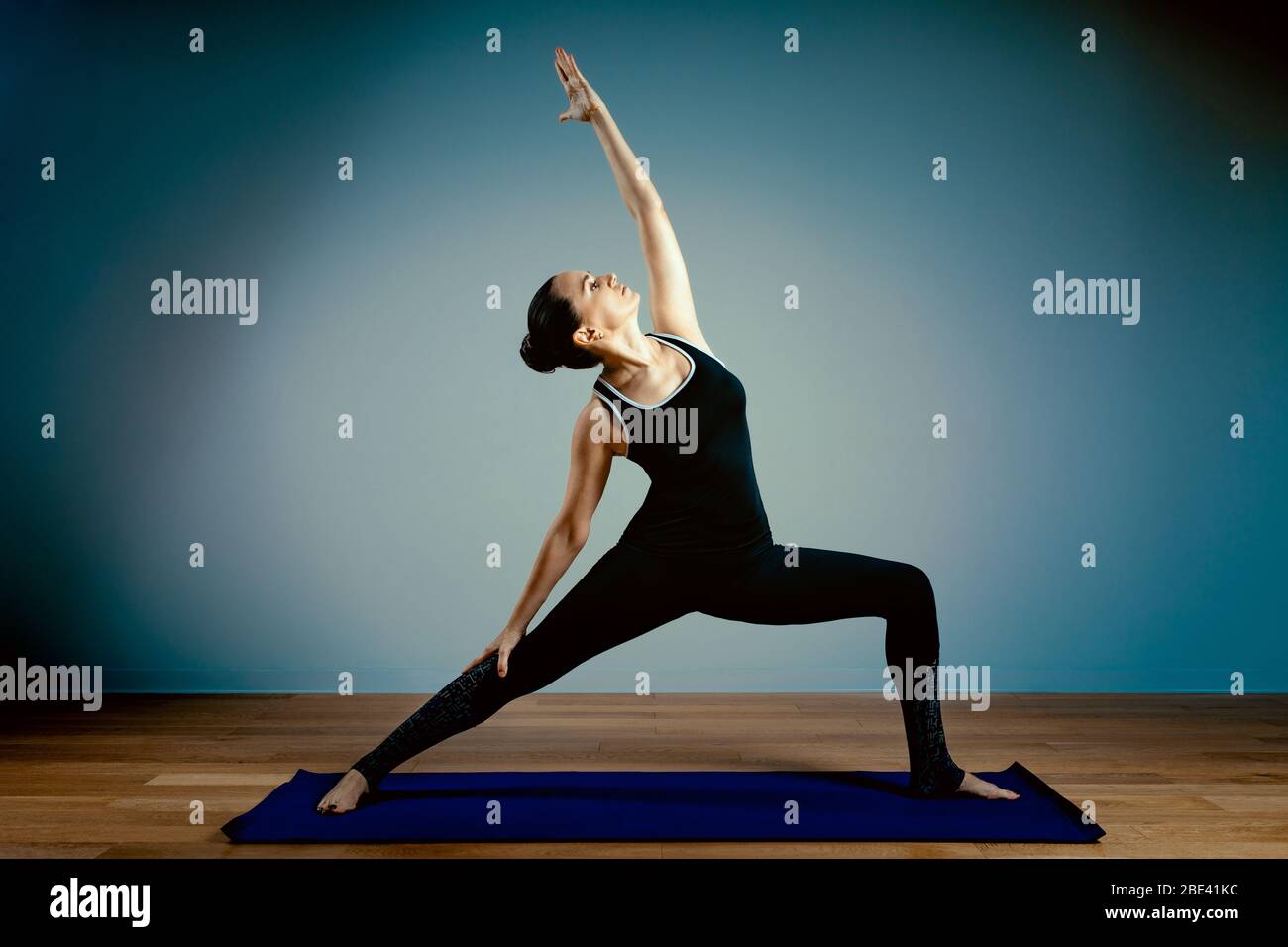 Adult woman 45-55 years old in good shape doing yoga posing on a blue ...