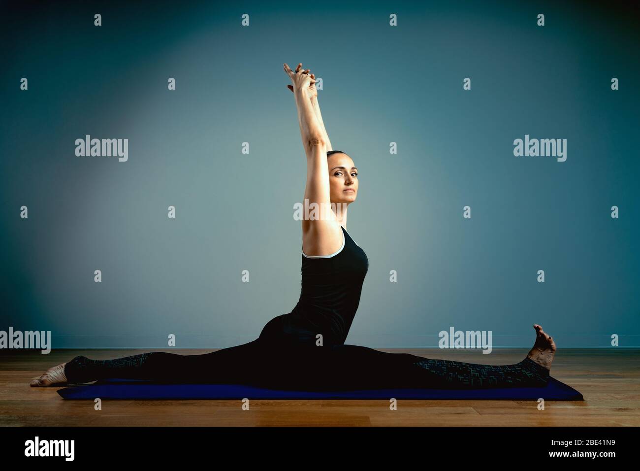 Adult woman 45-55 years old in good shape doing yoga posing on a blue ...