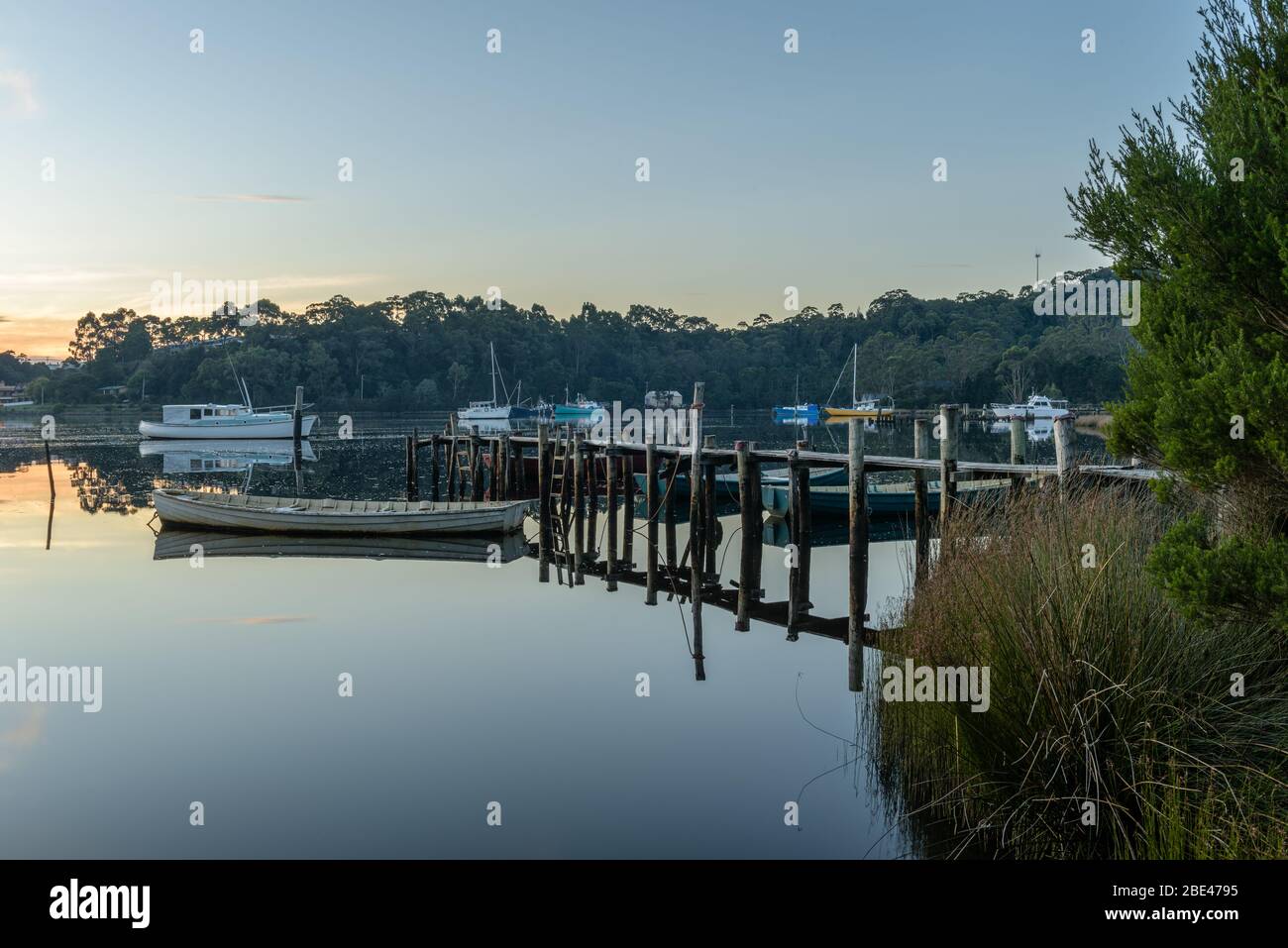 Traditional timber boats moored to a wooden jetty on Macquarie Harbour ...