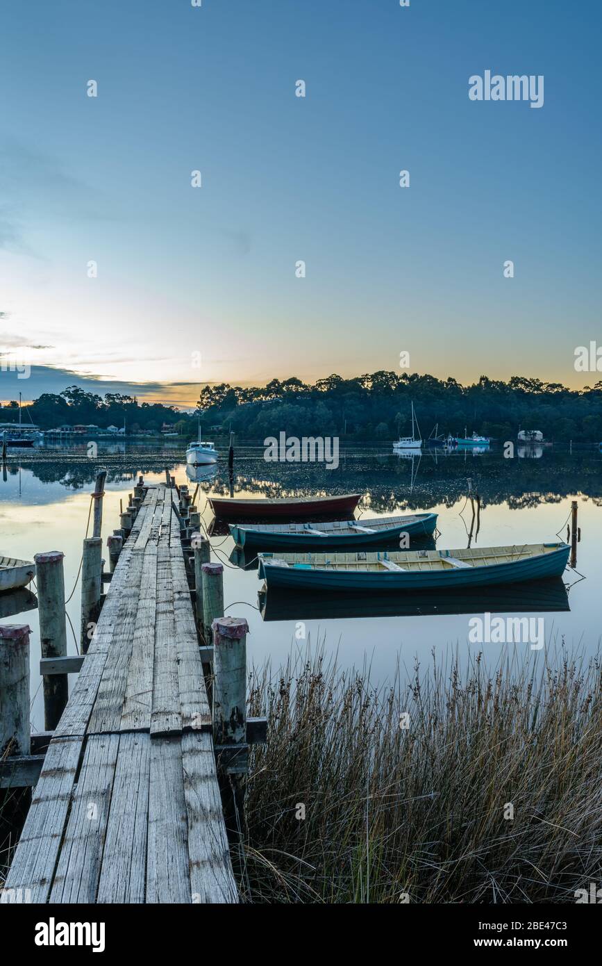 Traditional timber boats moored to a wooden jetty on Macquarie Harbour ...