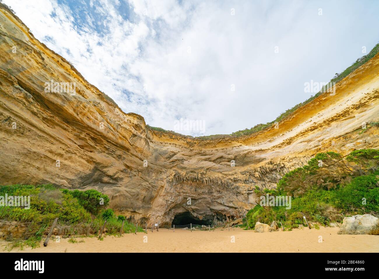 Horseshoe shaped limestone cliffs with stalactite cave at end on beach ...