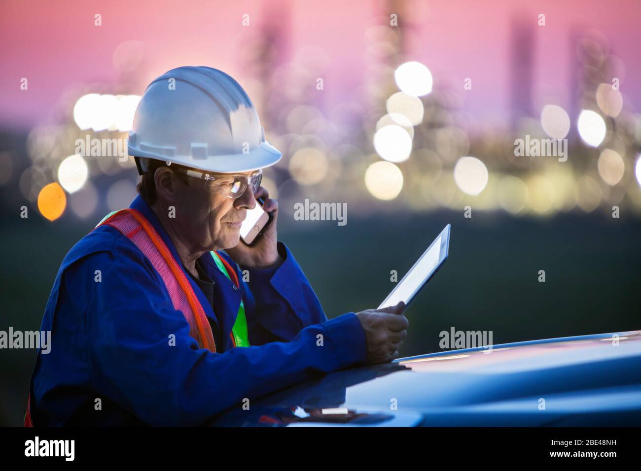 Man working on a tablet and smart phone with an oil refinery in the ...