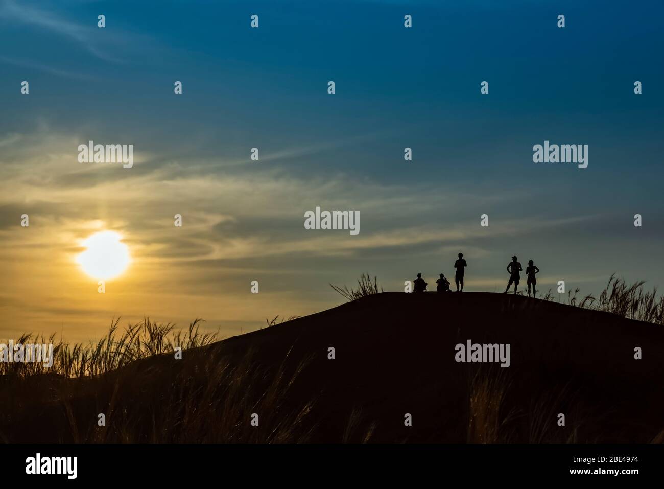 Silhouetted group of tourists stand looking out at the top of a sand ...