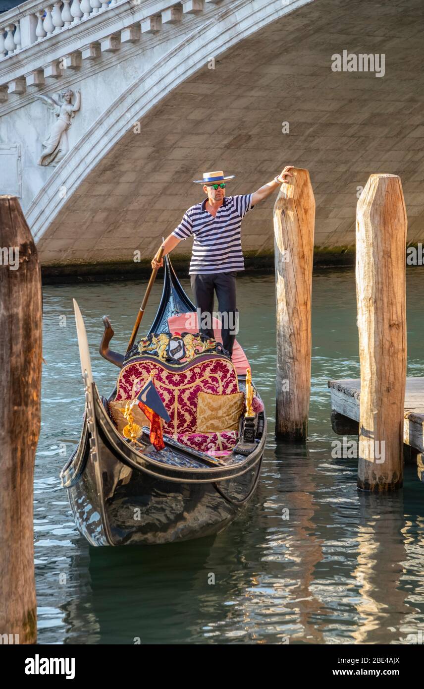 Gondolier stands on the back of a gondola at the waterfront waiting for ...