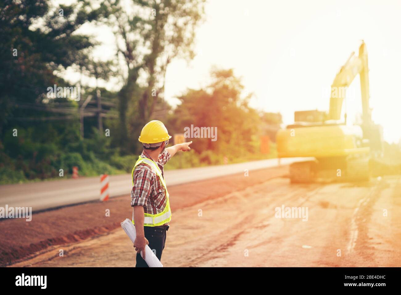 engineer holding blueprint at road construction site with machinery ...