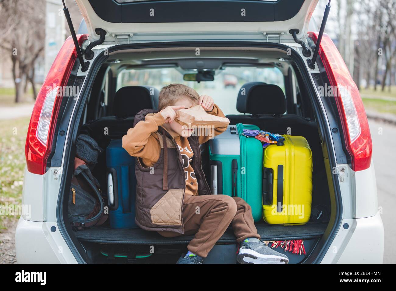little kid looking into paper bag with candies sitting in car trunk ...