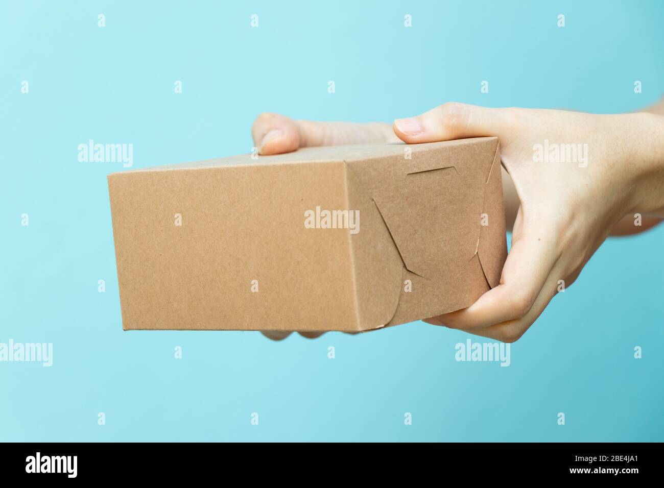 Woman hand hold the brown corrugated box on blue wall background with ...