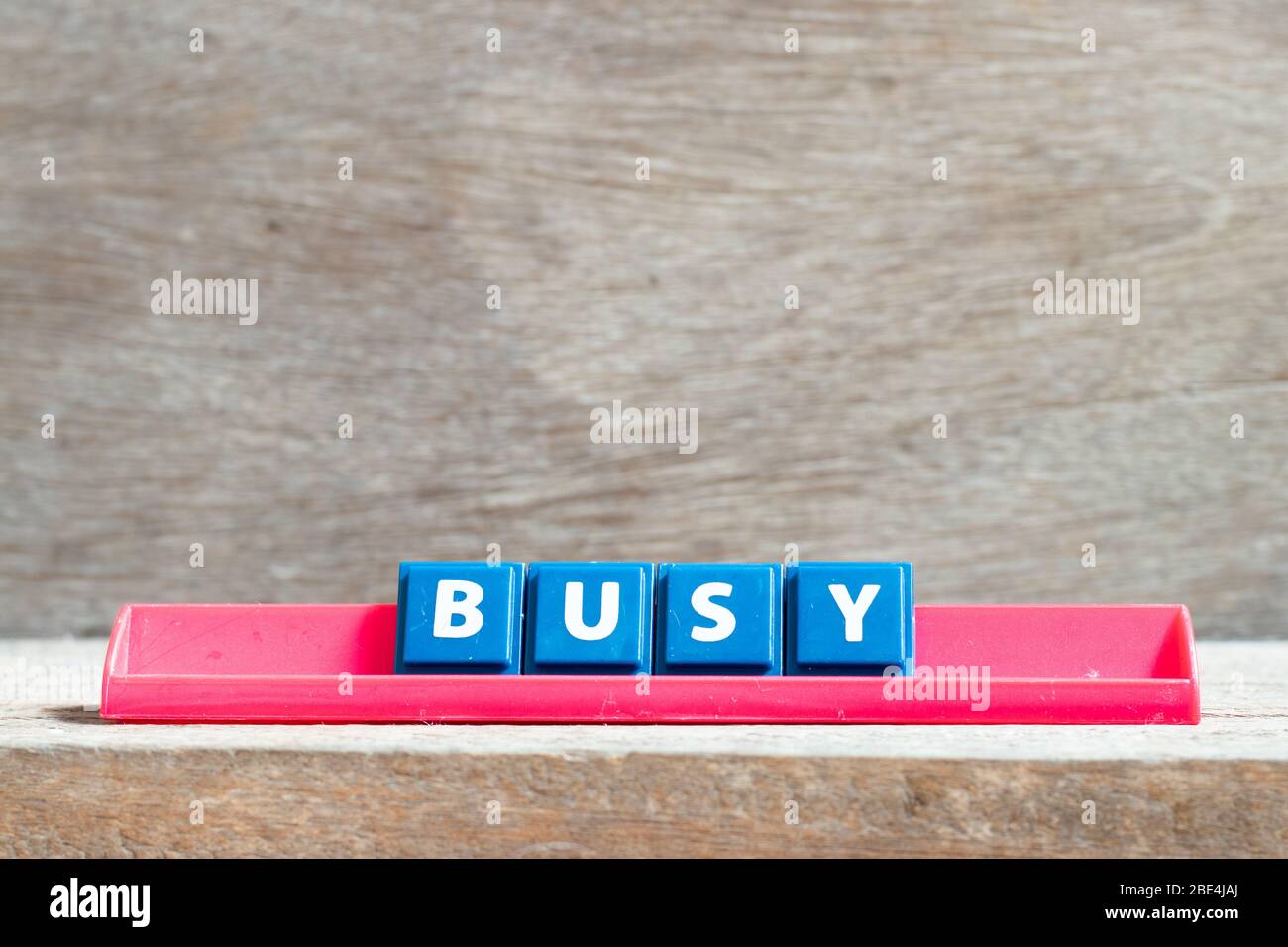 Tile letter on red rack in word busy on wood background Stock Photo - Alamy