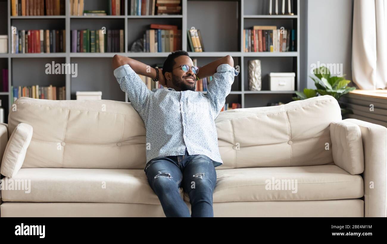 Peaceful young african american man stretching back, relaxing on couch ...