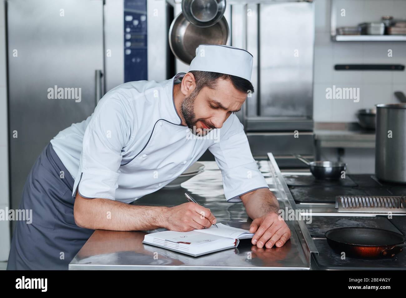 Concentrated male chef cook with grocery list or bills doing inventory ...