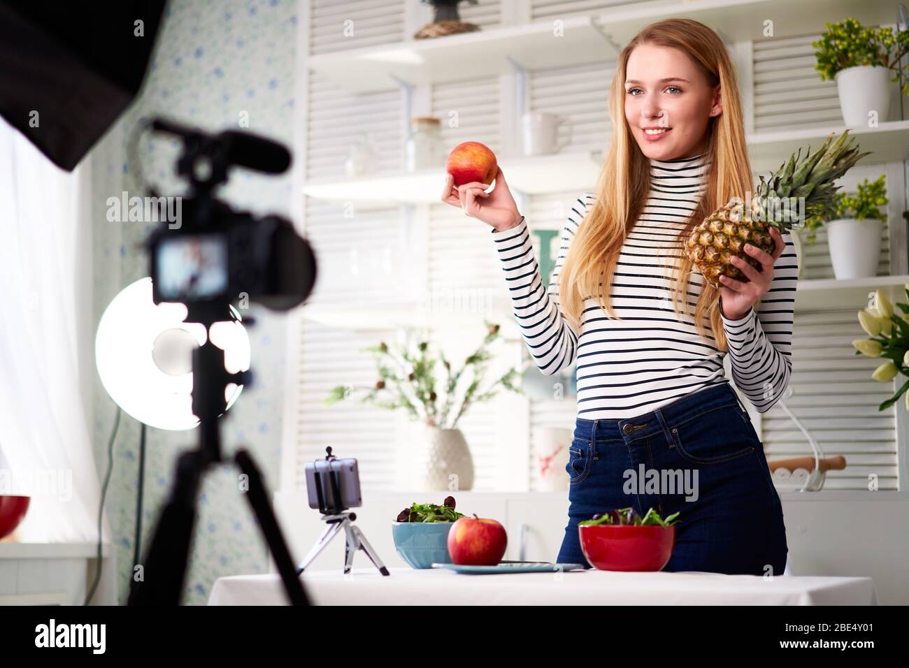 Food blogger cooking fresh vegan salad of fruits in kitchen studio ...