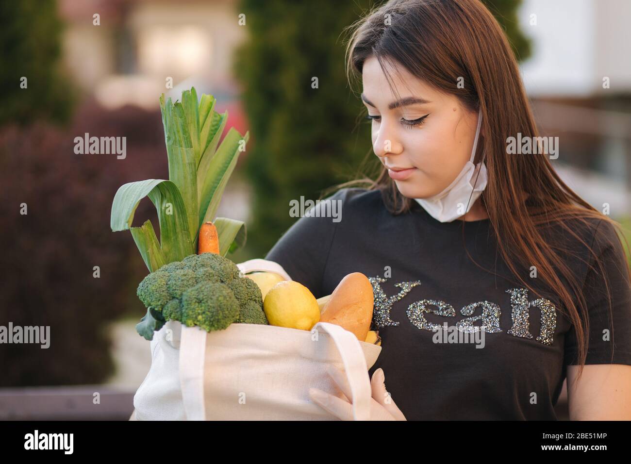 Young woman in mask and gloves hold bag with fresh food, vegetables ...