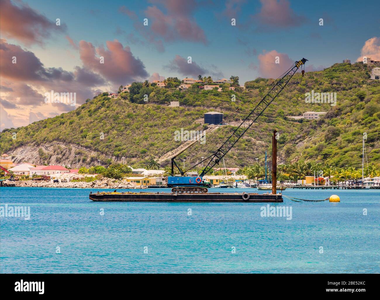 A blue crane on a working barge over blue water in the harbor of ...
