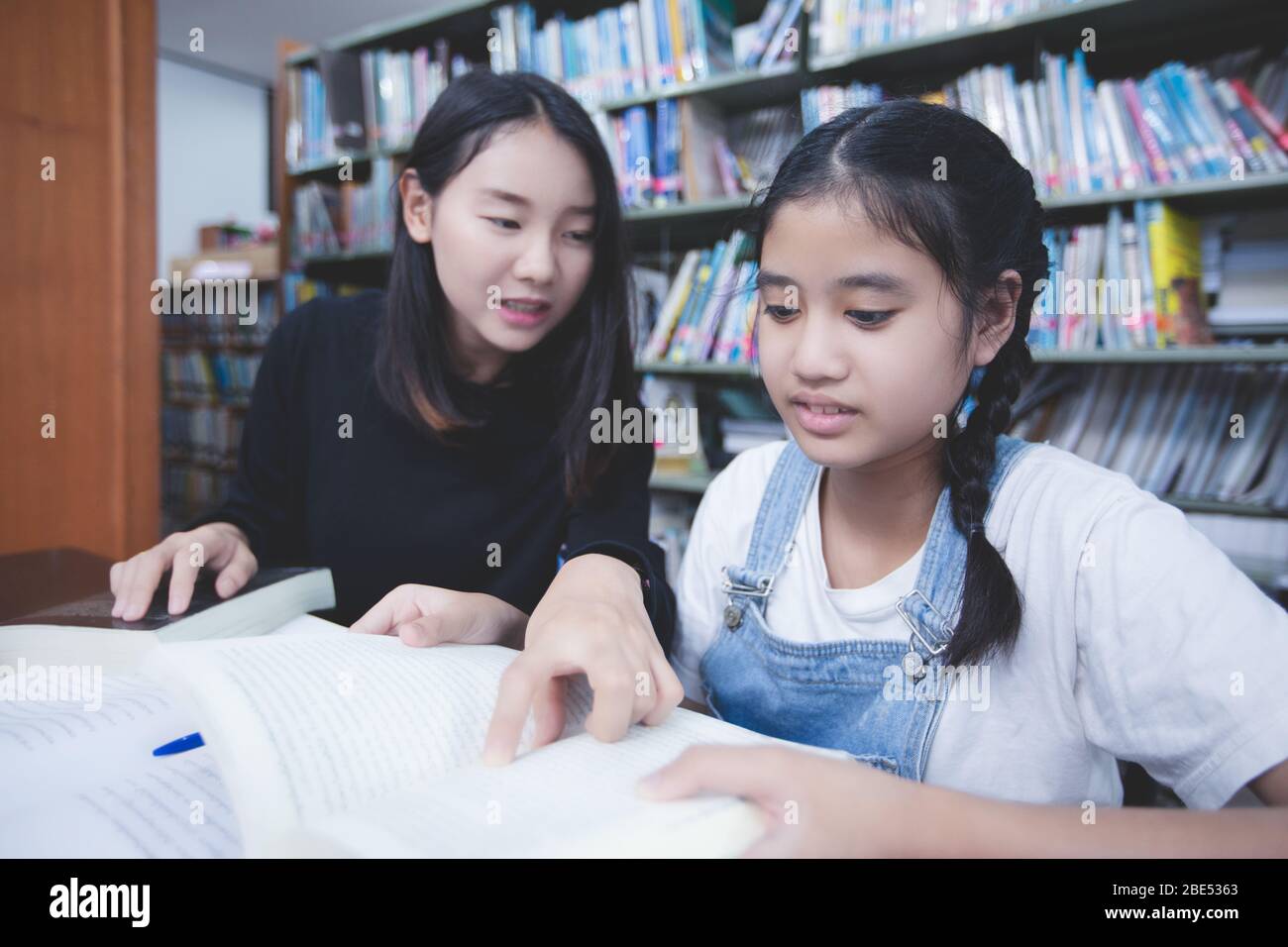 Two Asian girl students reading books and using notebook in the library ...